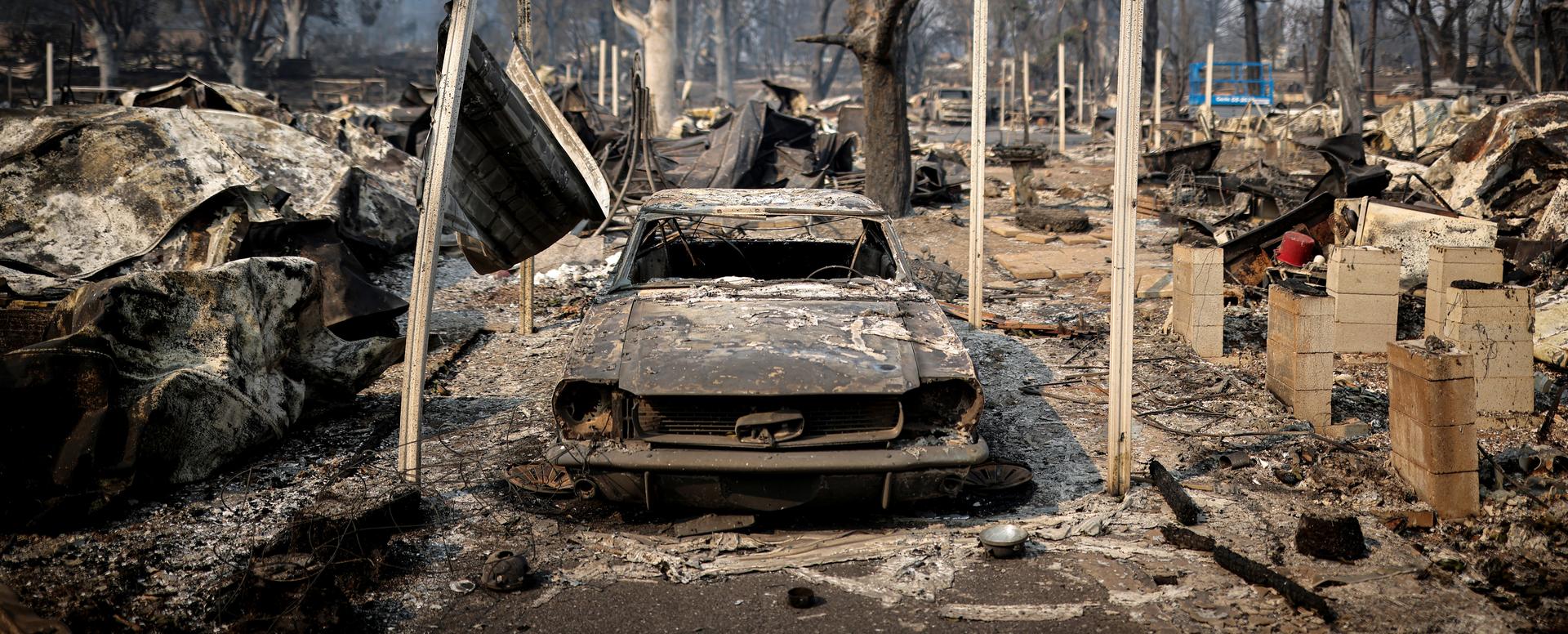 Burned car is seen in a neighborhood after wildfires destroyed an area ...